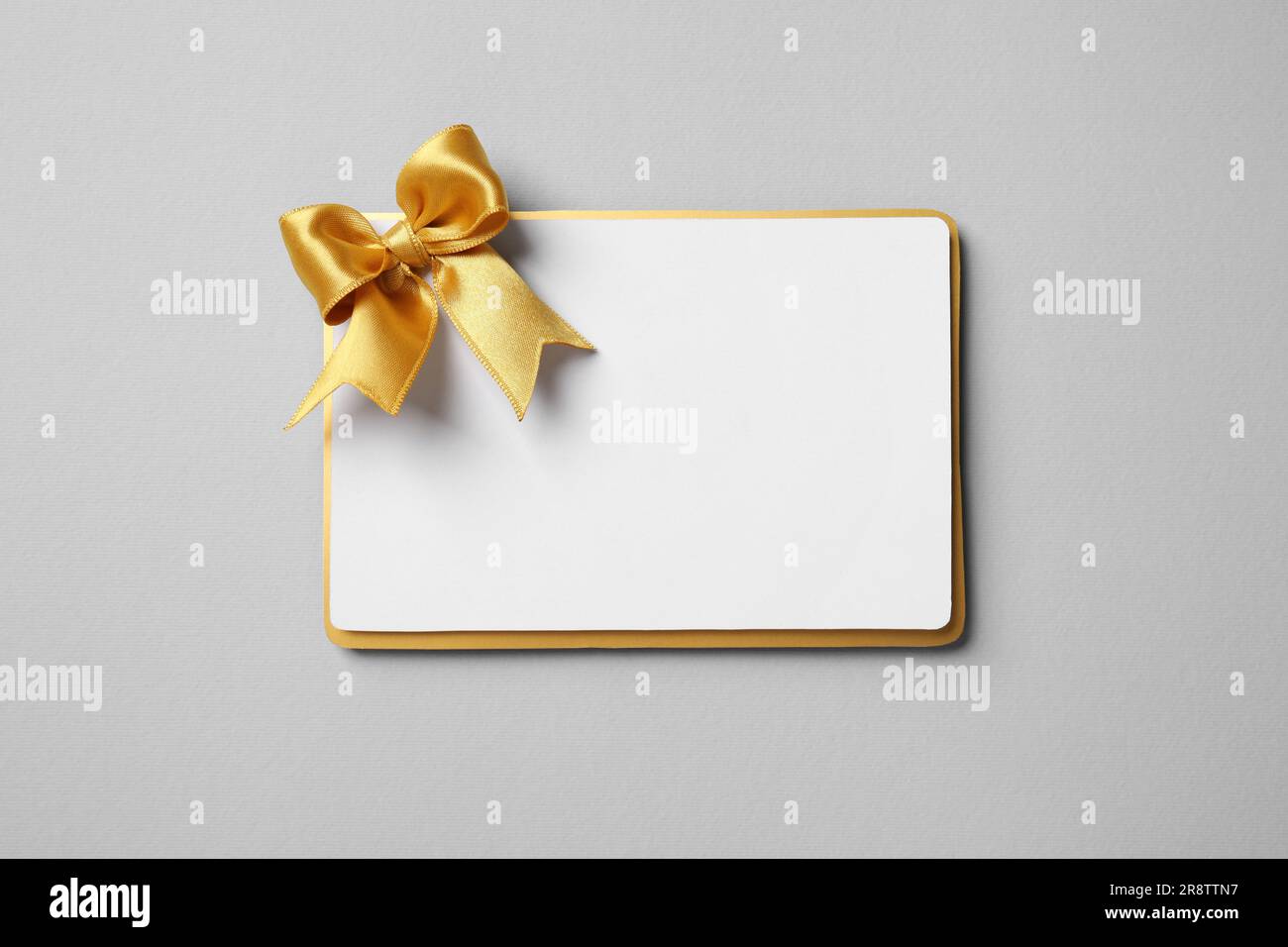 Blank gift card with golden bow on light grey background, top view ...