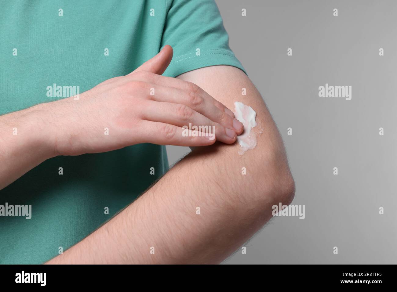 Man applying ointment onto his arm on light grey background, closeup ...