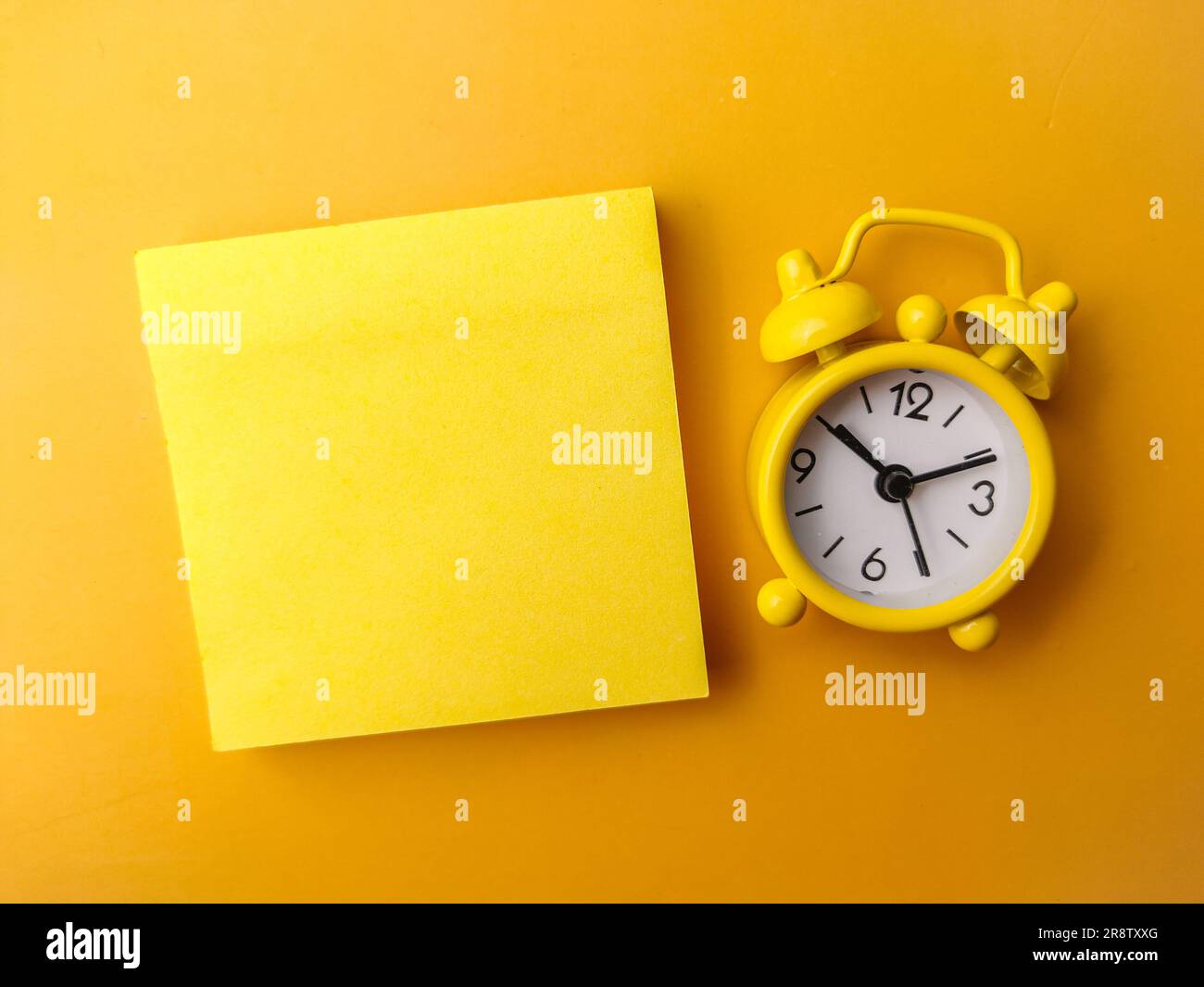 Closeup yellow sticky note with alarm clock on a yellow background with ...