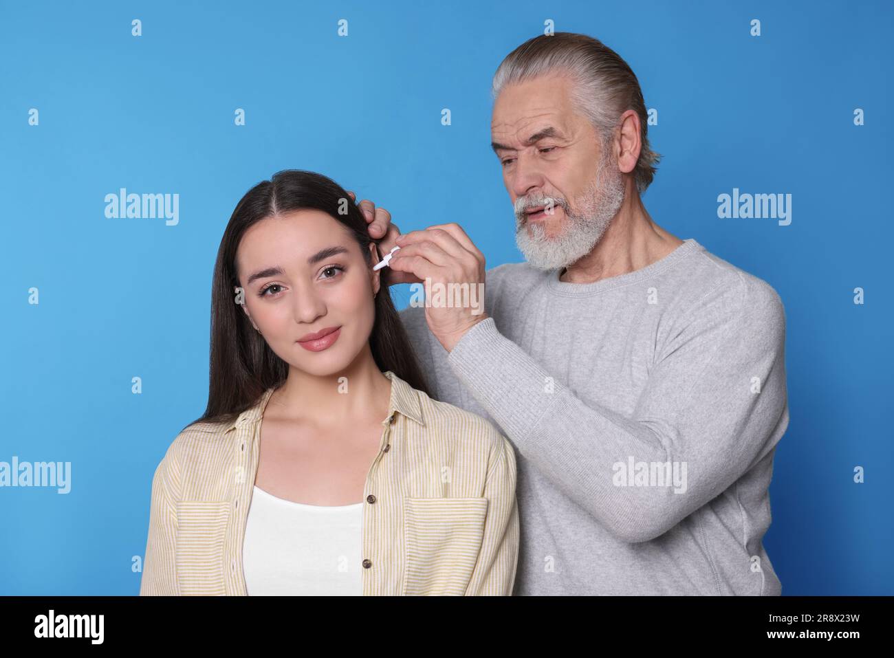 Senior man dripping medication into woman's ear on light blue ...