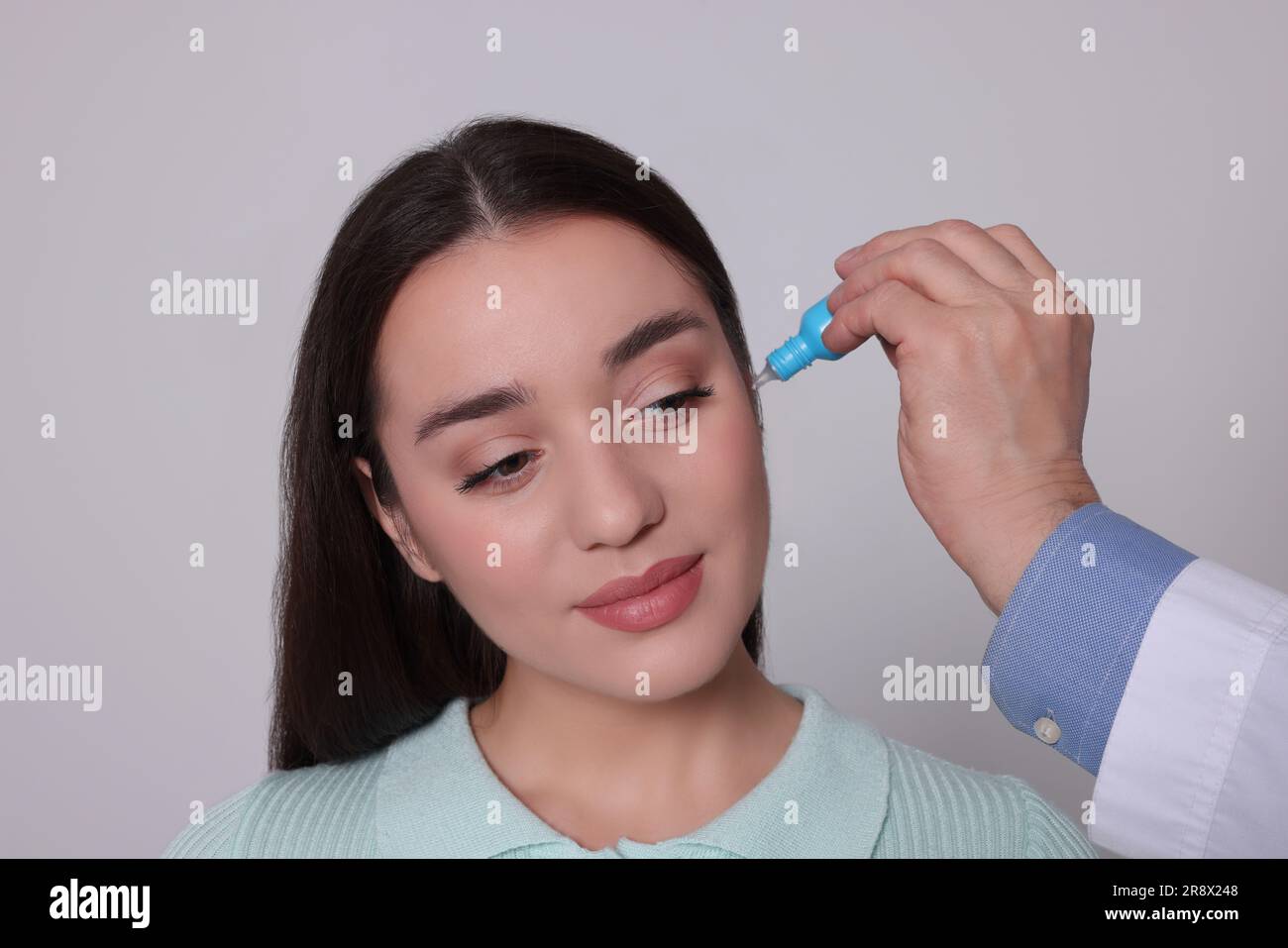 Doctor dripping medication into woman's ear on light grey background ...