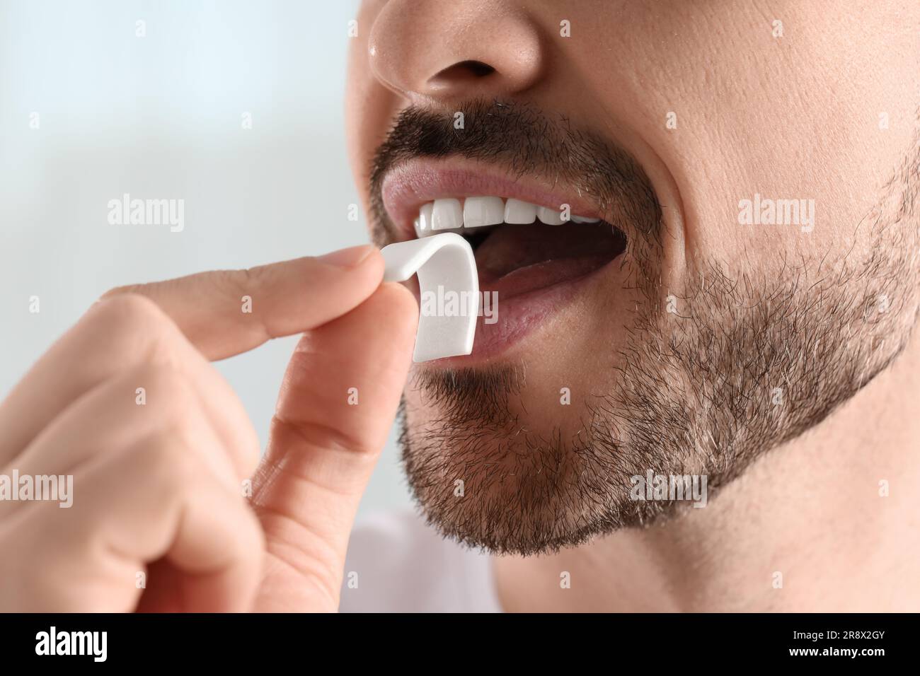 Man putting chewing gum into mouth on light background, closeup Stock ...