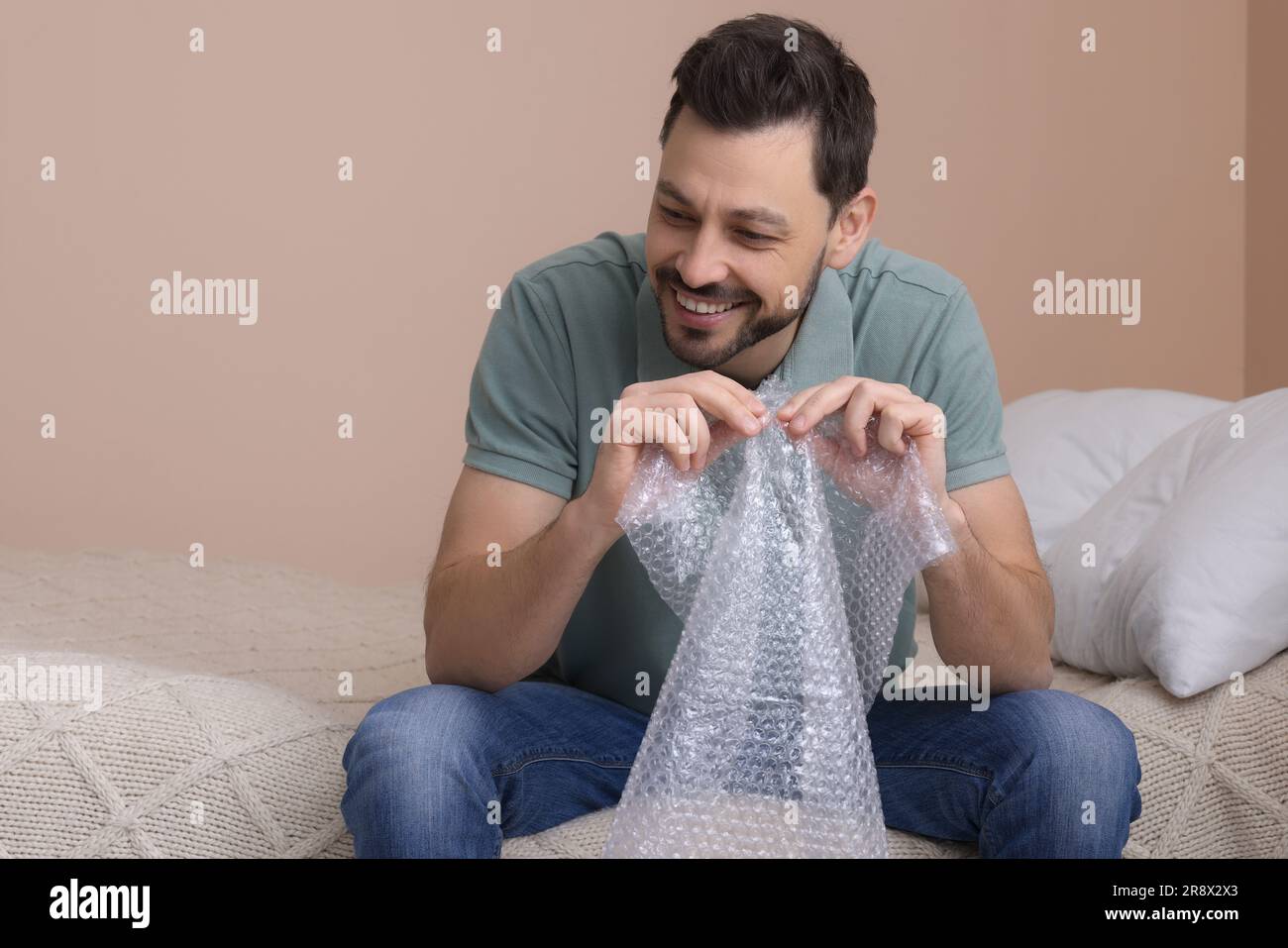 Man popping bubble wrap in bedroom at home. Stress relief Stock Photo ...