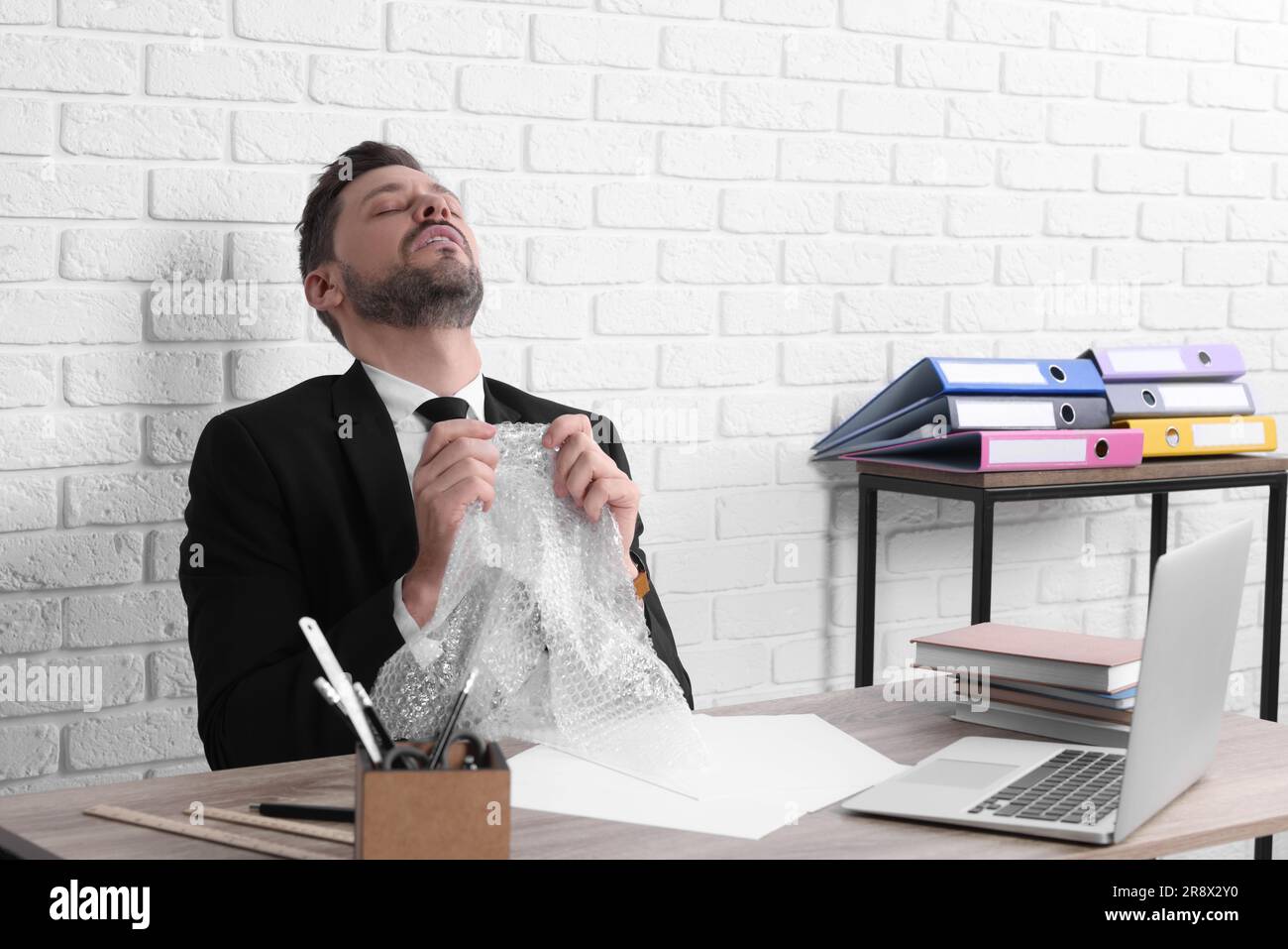Businessman popping bubble wrap at workplace in office. Stress relief ...