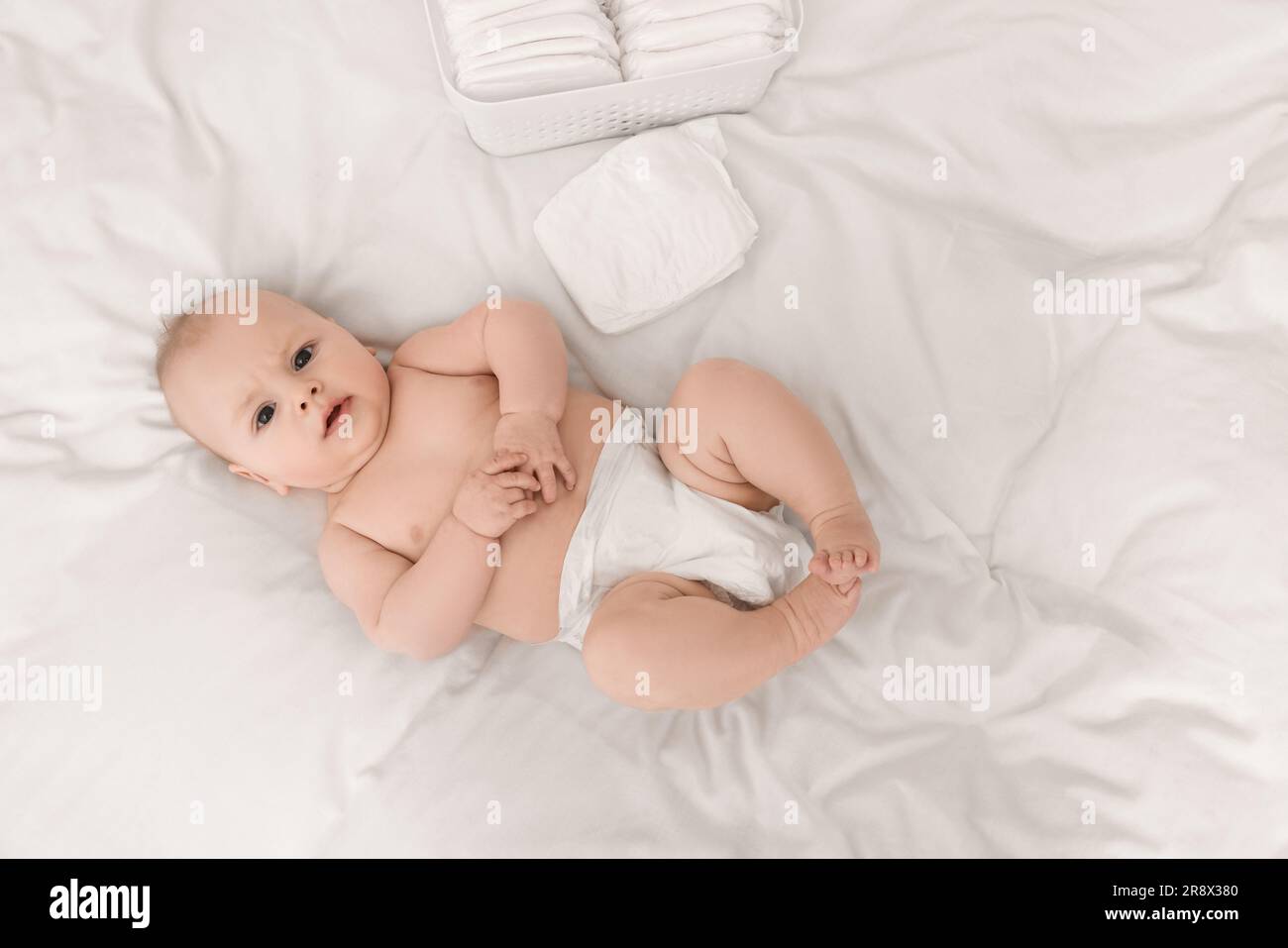 Cute baby and diapers on white bed, top view Stock Photo - Alamy