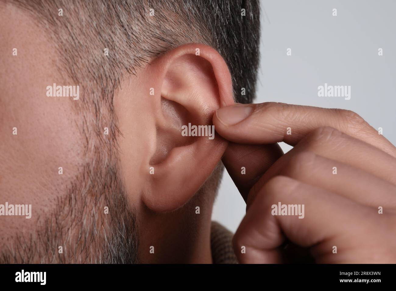 Man touching his ear on light grey background, closeup Stock Photo - Alamy