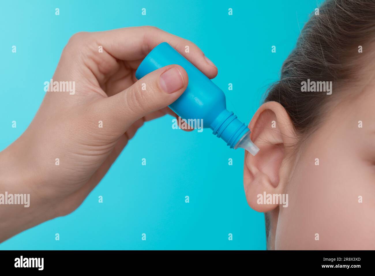 Mother dripping medication into daughter's ear on light blue background ...
