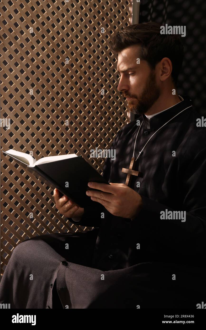 Catholic priest in cassock reading Bible in confessional booth Stock ...