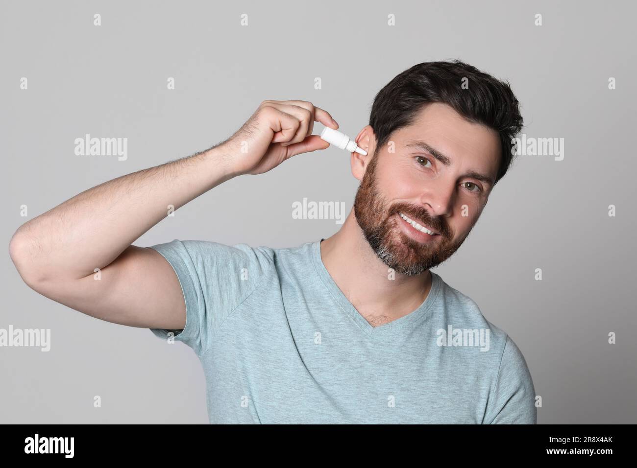 Man using ear drops on grey background Stock Photo - Alamy