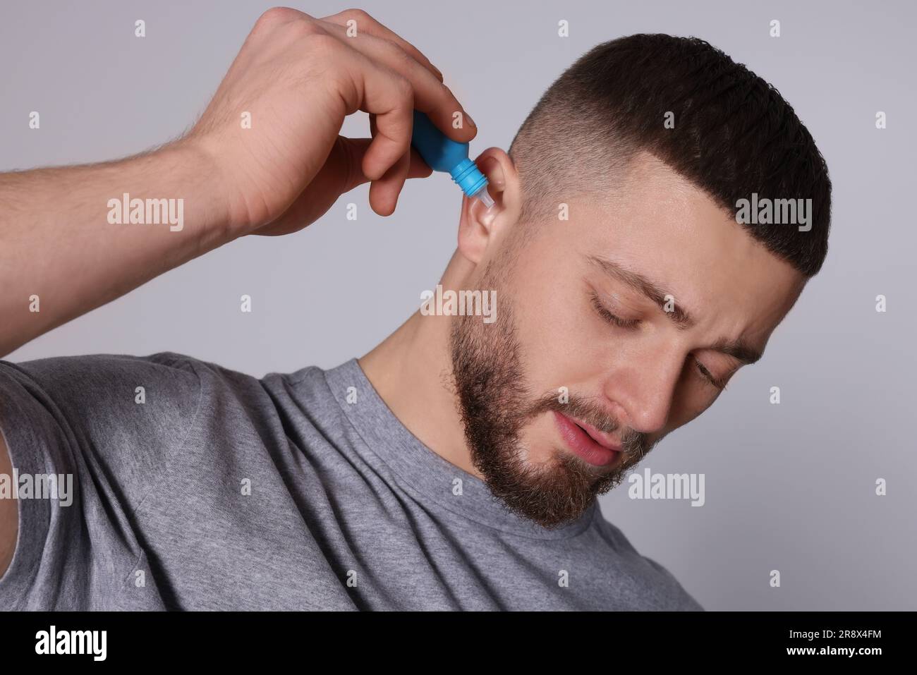 Man using ear drops on light grey background Stock Photo - Alamy