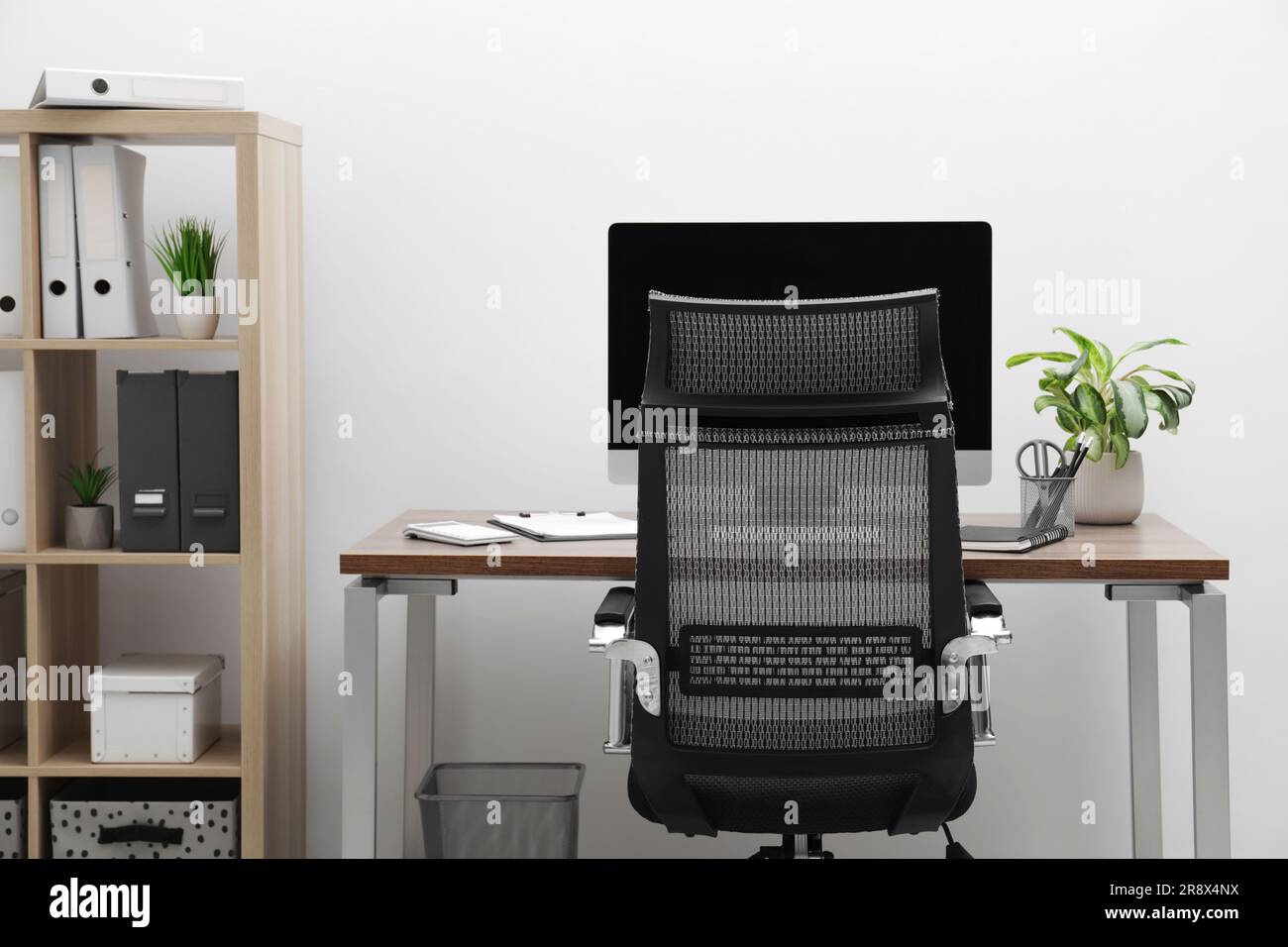 Cozy workspace with computer on desk, chair and bookcase near white ...