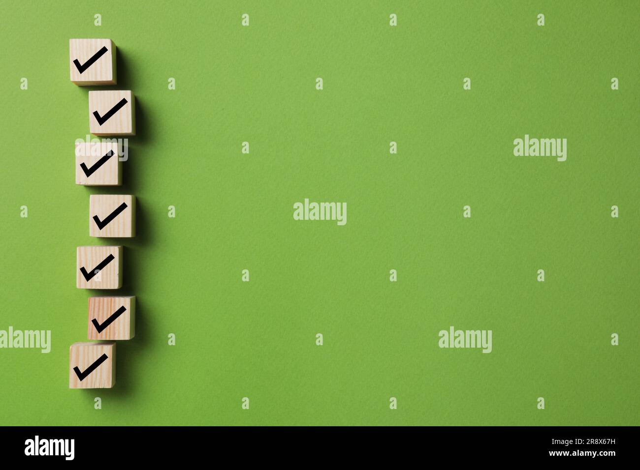 Wooden cubes with check marks on green background, flat lay. Space for ...
