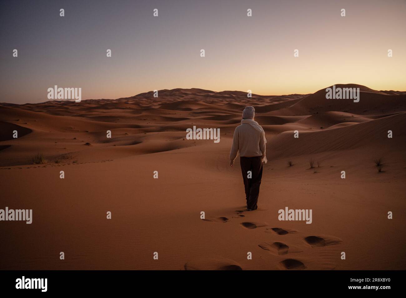A hooded figure silhouetted against the golden sky at sunset, walking ...