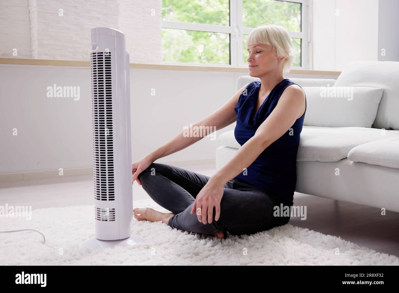 Young Woman Cooling Herself During Hot Weather In Front Of Fan At Home ...