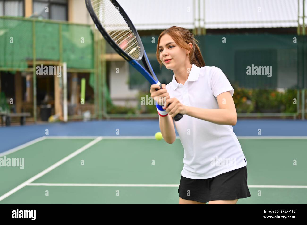 Joyful young woman hitting ball with racket to return ball over net ...