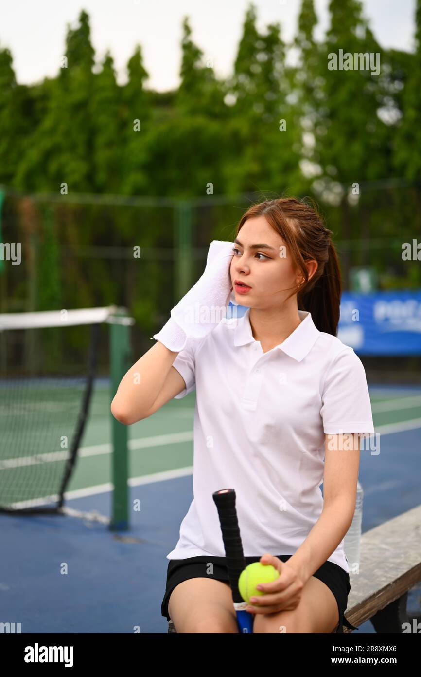 Image of tired female tennis player wiping sweat with towel, resting on ...