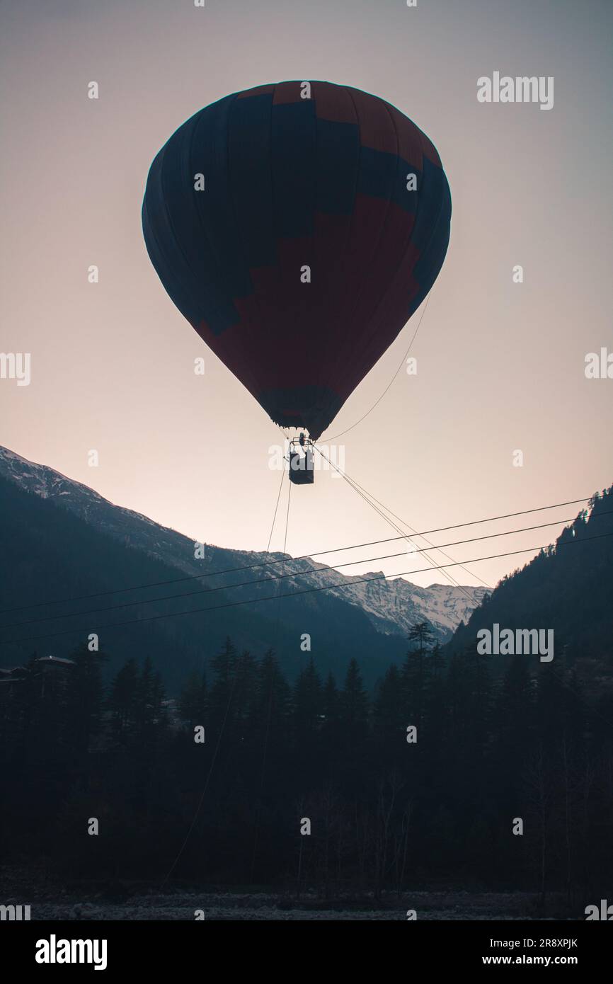 A colorful hot air balloon drifting in the sky, surrounded by mountains ...