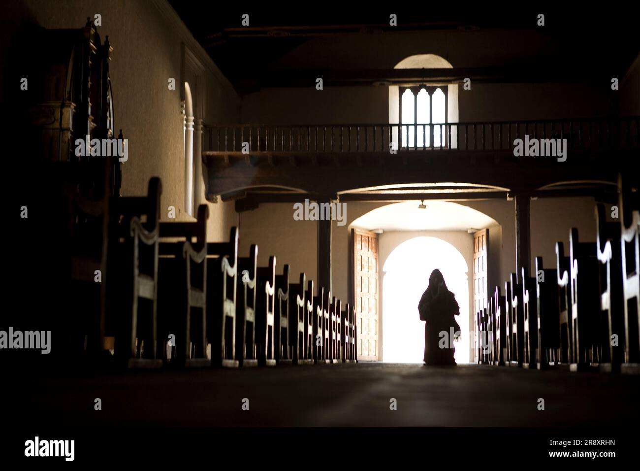 Light beams into a church as a woman enters praying on her knees in ...