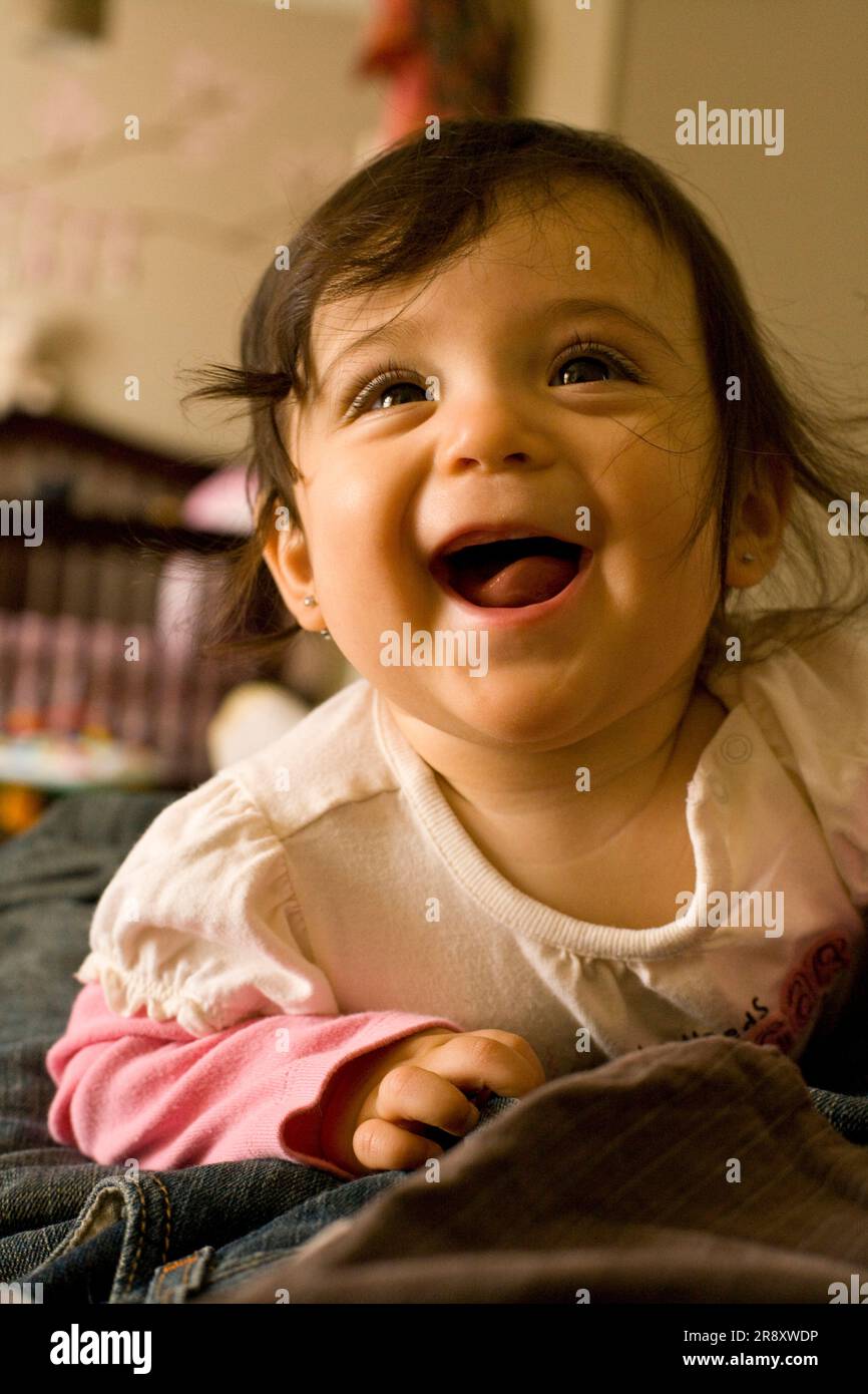A giddy, brown haired baby girl giggles while lying on her stomach ...