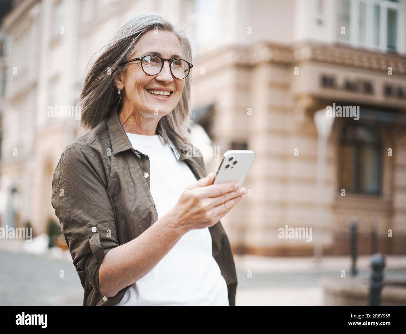 Old caucasian woman texting message on mobile phone while standing on ...