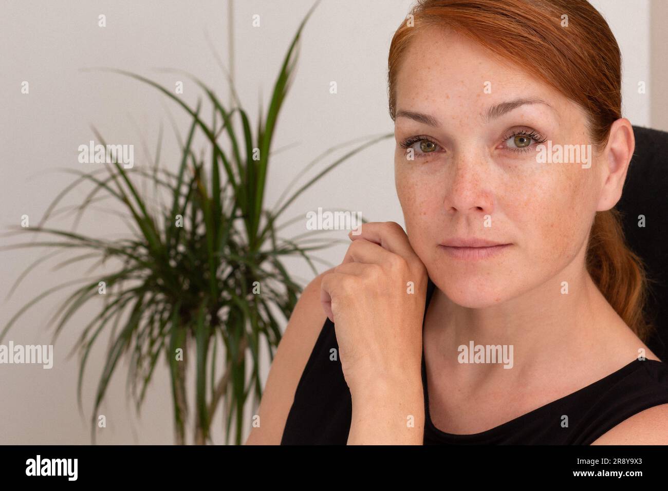 Portrait of caucasian middle aged woman in chair with freckles and reddish hair with calm look ...