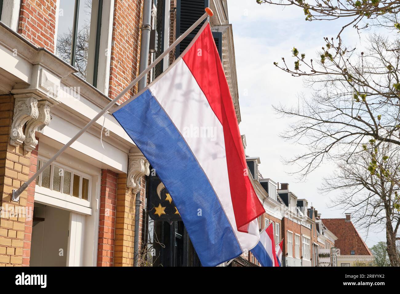 Dutch flags waving in a typical dutch street on Koningsdag under a blue ...