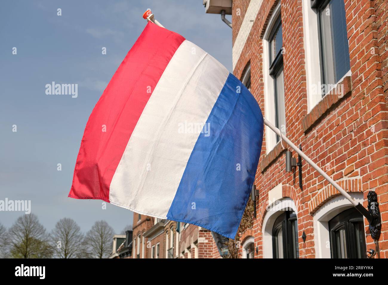 Dutch flag waving in a typical dutch street on Koningsdag under a blue ...