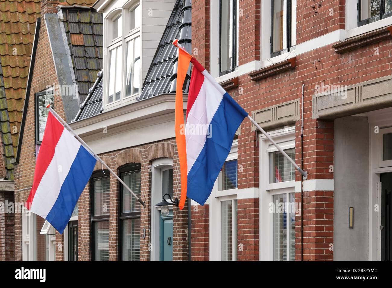 Dutch flags with orange streamer waving in a typical dutch street on ...