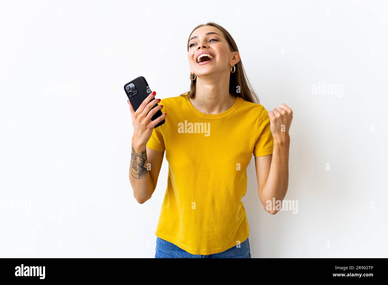 Portrait of a happy joyful girl holding mobile phone and celebrating a ...