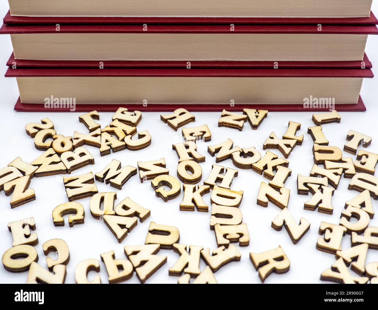 A stack of wooden alphabet letters in front of books on a white ...