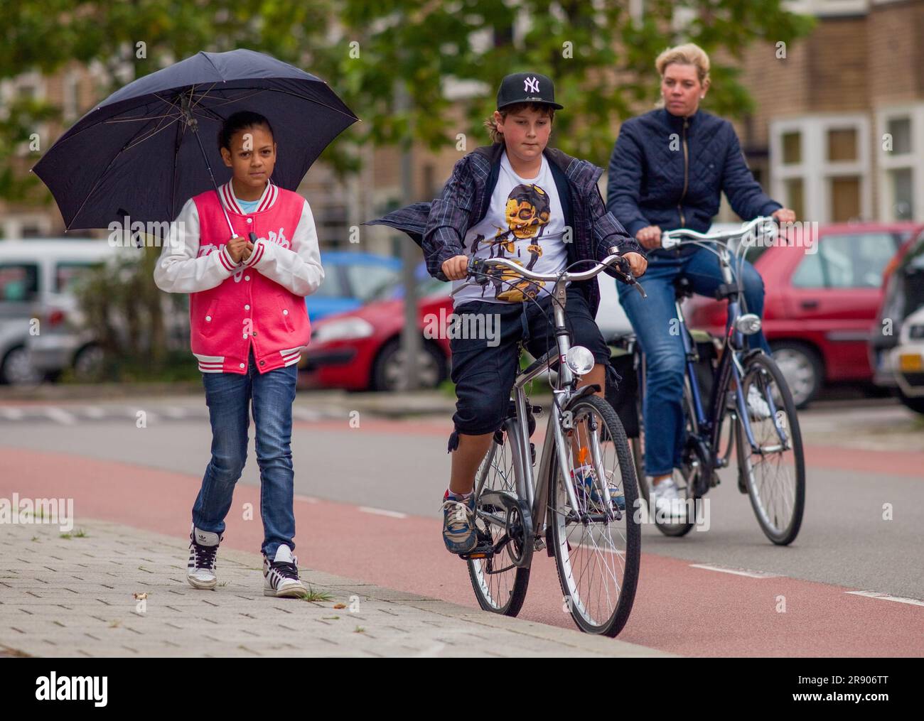 Netherlands, children on the road, walking with an umbrella and cycling ...