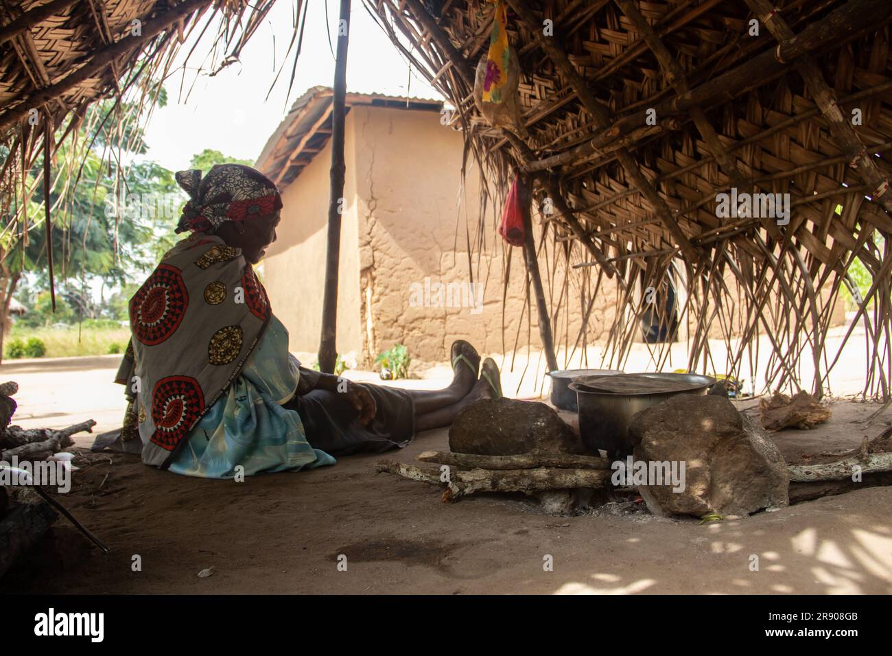 Old lady from Makonde tribe sitting in primitive kitchen and preparing ...