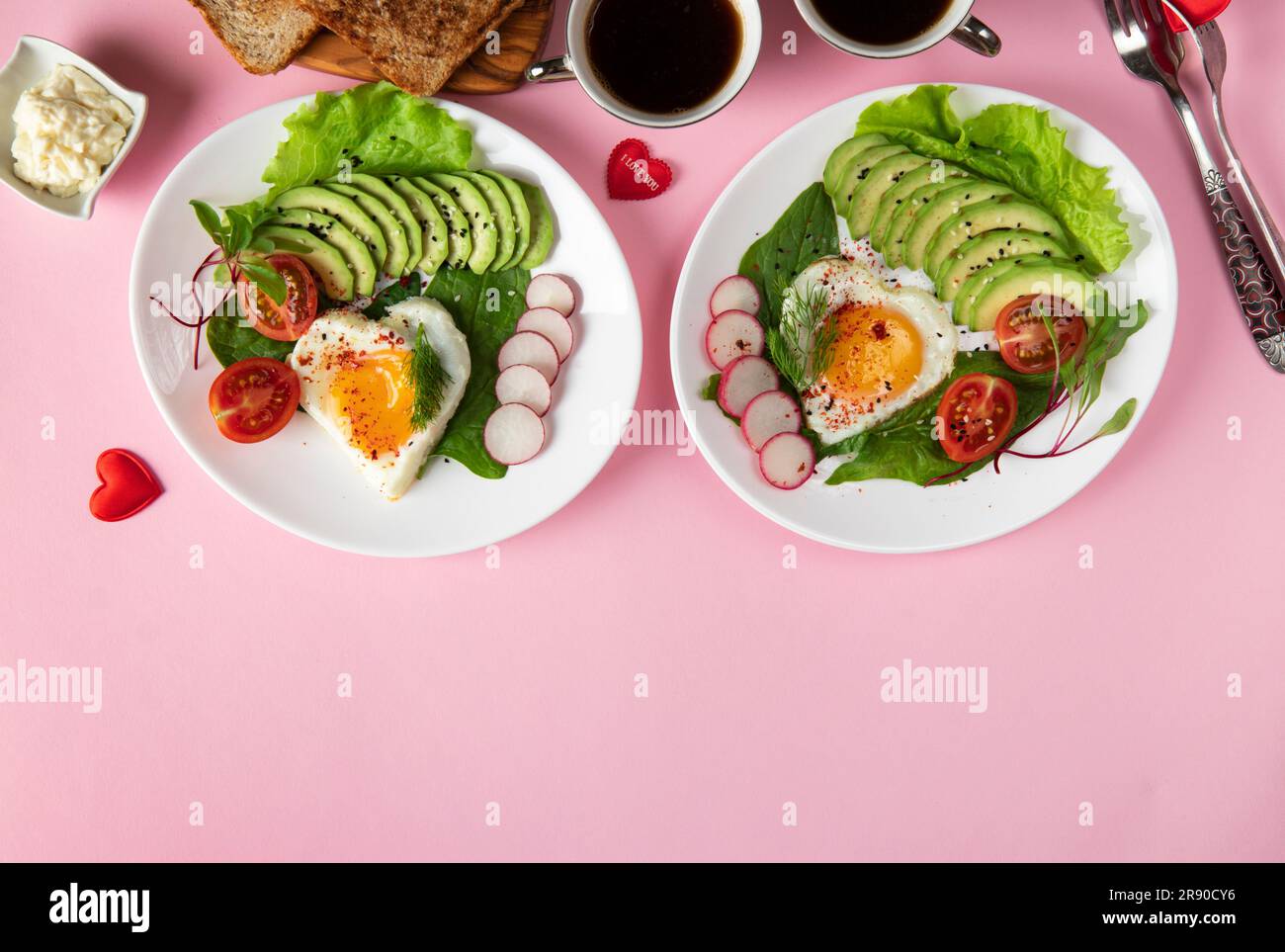 Romantic couple breakfast - two portions heart-shaped fried eggs with avocado, spinach, cherry ...