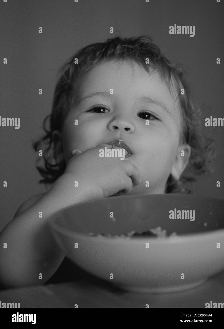 Funny baby eating food himself with a spoon on kitchen. Funny child ...