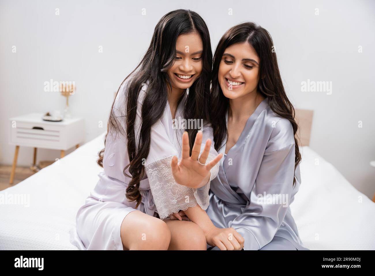 happy asian woman and her friend sitting on bed, showing engagement ...