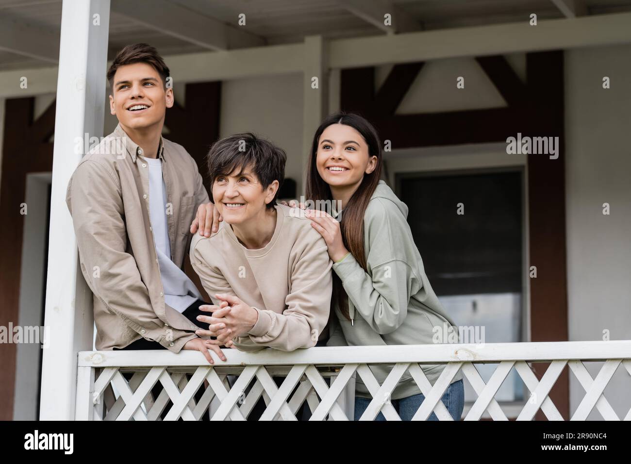 Positive siblings looking away while hugging middle aged mother and ...