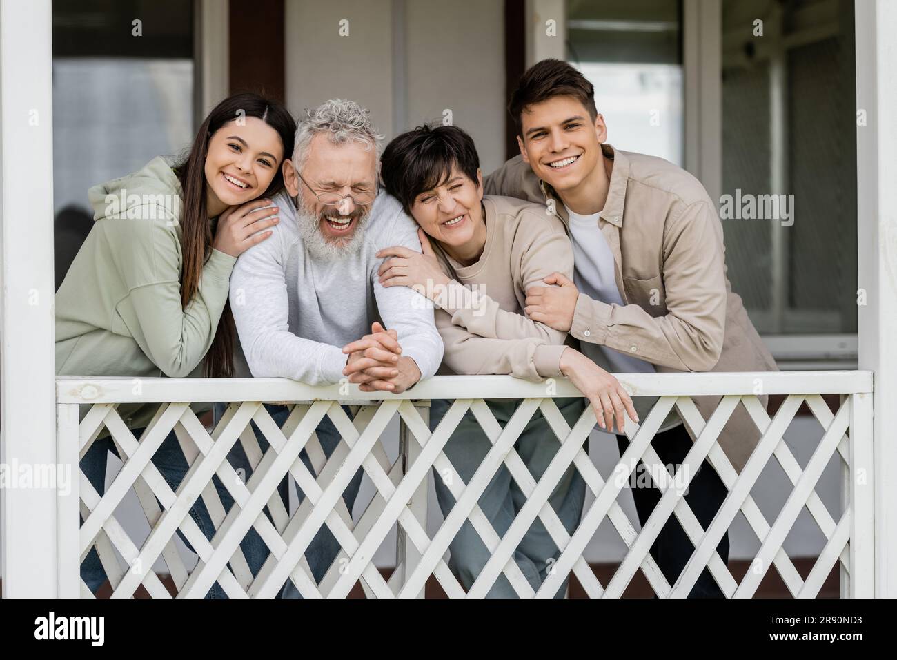 parents day, middle aged parents hugging with teenage daughter and young adult son on porch of ...