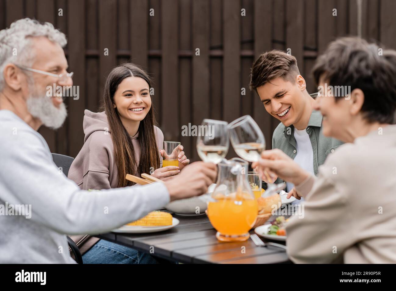 Smiling siblings sitting near tasty bbq food and blurred middle aged ...
