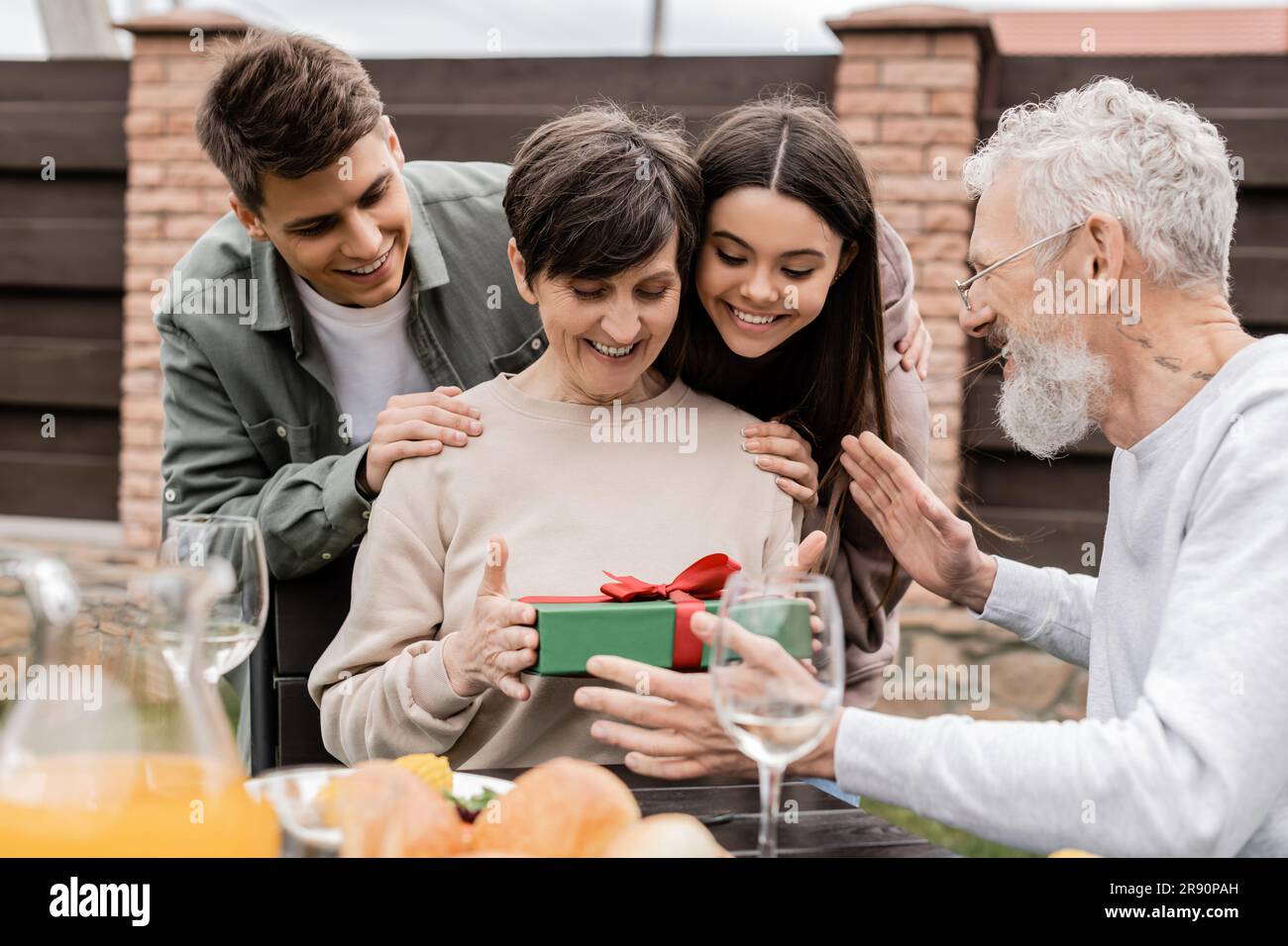Smiling children hugging middle aged mother with gift box and father ...