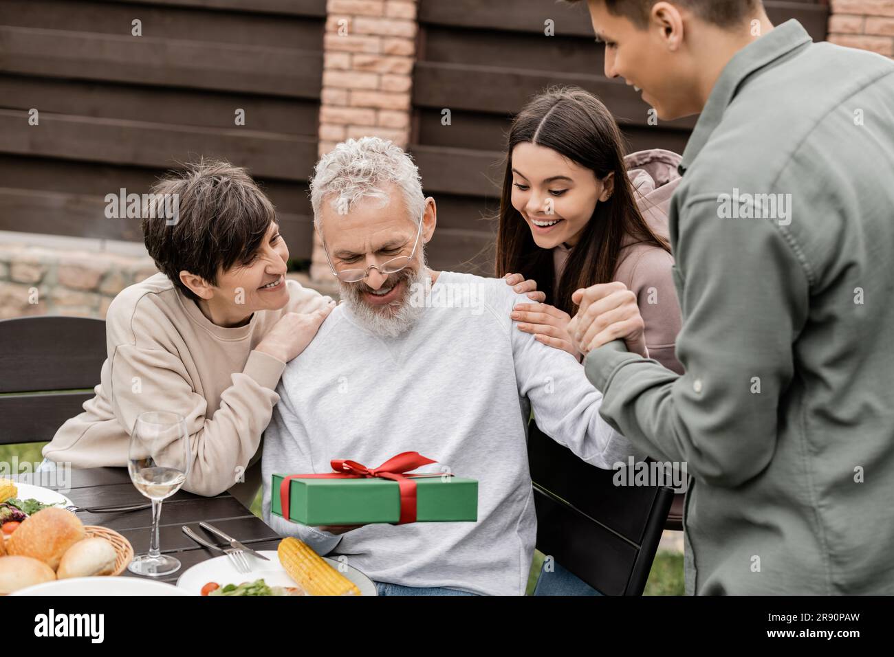 Smiling middle aged man holding gift box near children and wife during ...