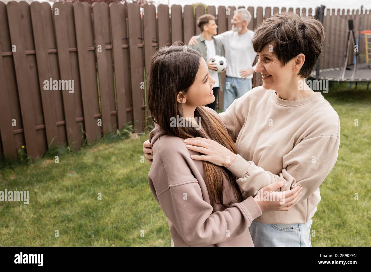 Positive teenage girl hugging middle aged mom near blurred family with ...