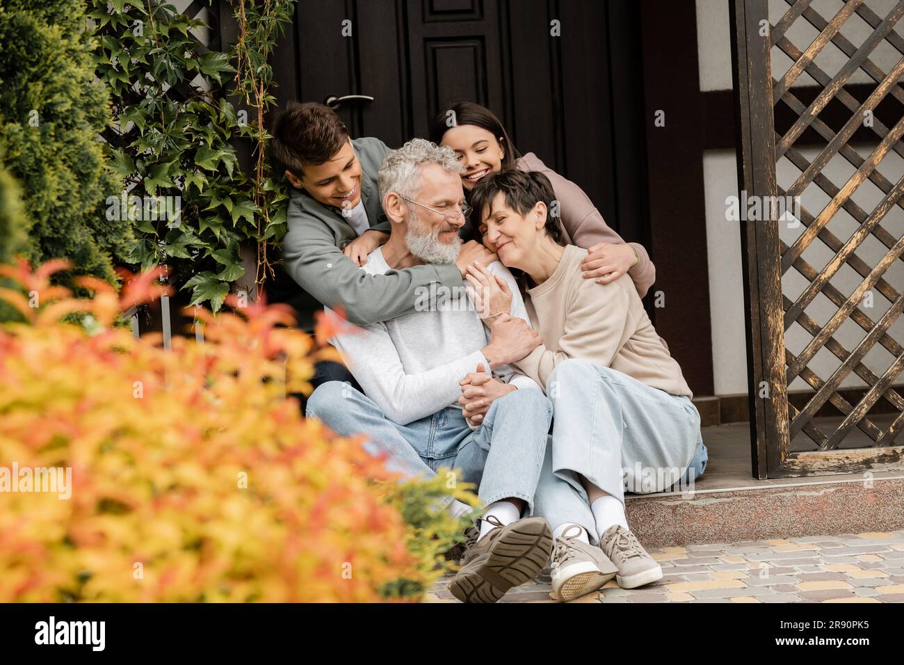 Smiling children hugging happy middle aged parents while sitting on ...