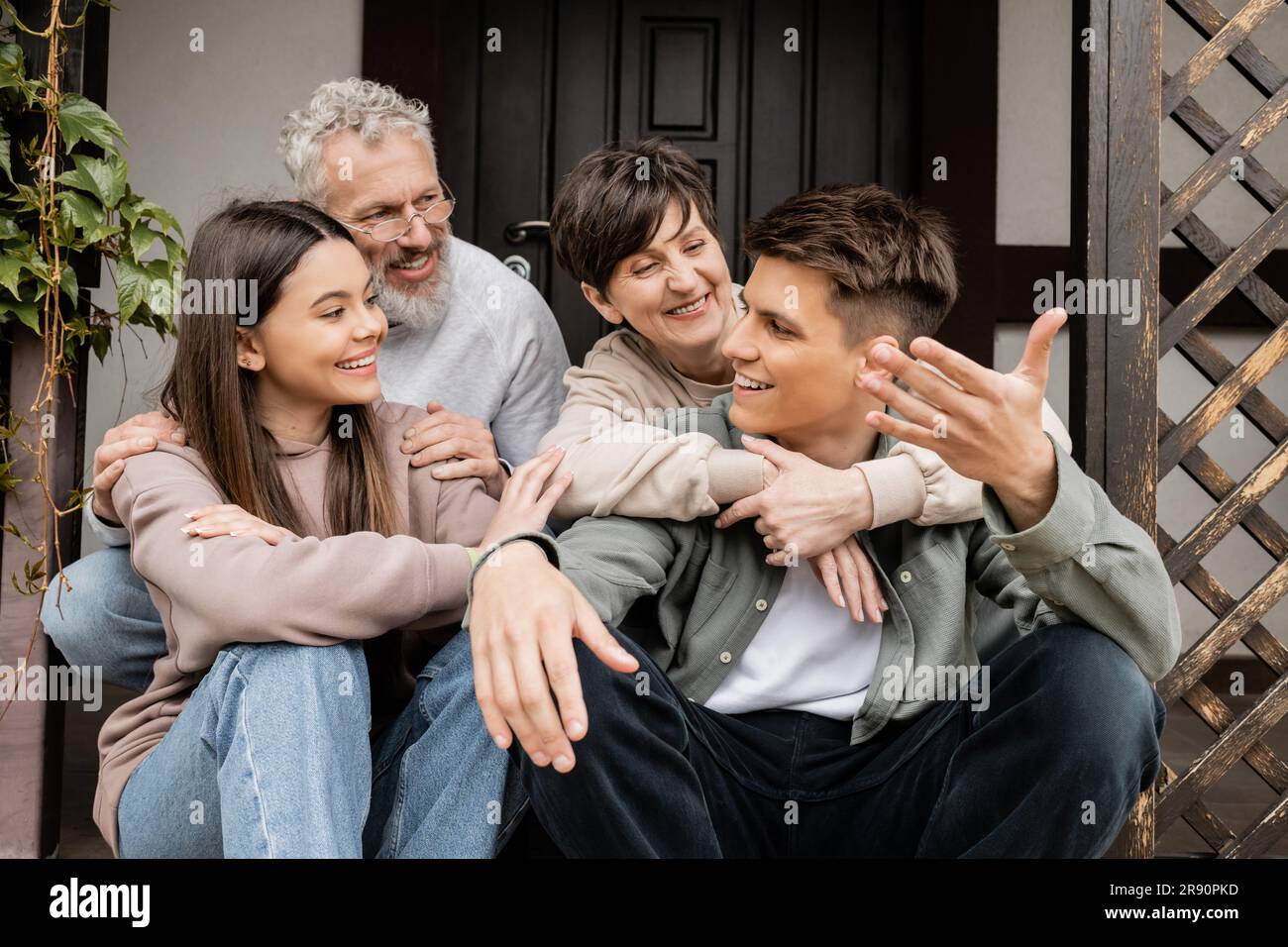 Smiling young man talking to family and sister while sitting on porch ...