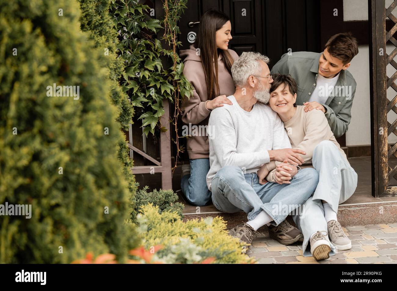 Smiling middle aged parents holding hands while sitting on porch of ...