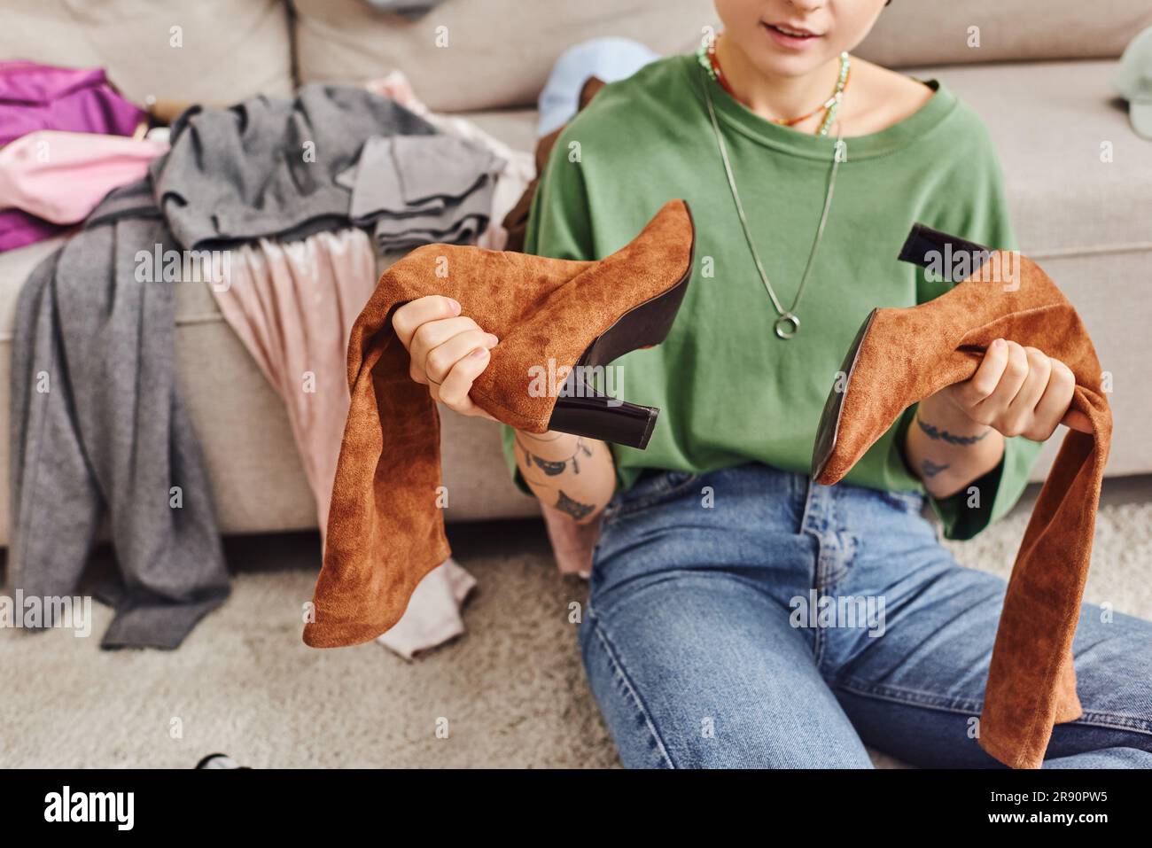 partial view of young tattooed woman in casual clothes sitting on floor ...