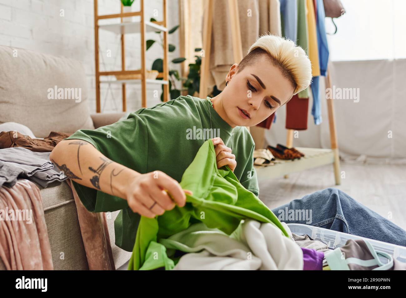 young, stylish and tattooed woman holding green garment in modern ...