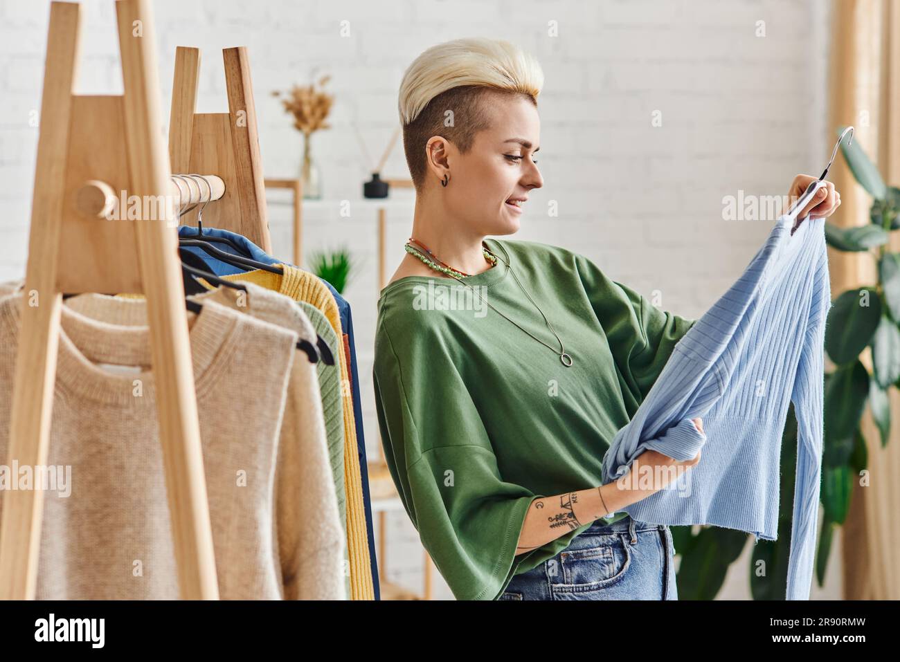 clothing sorting, side view of trendy and tattooed woman looking at ...