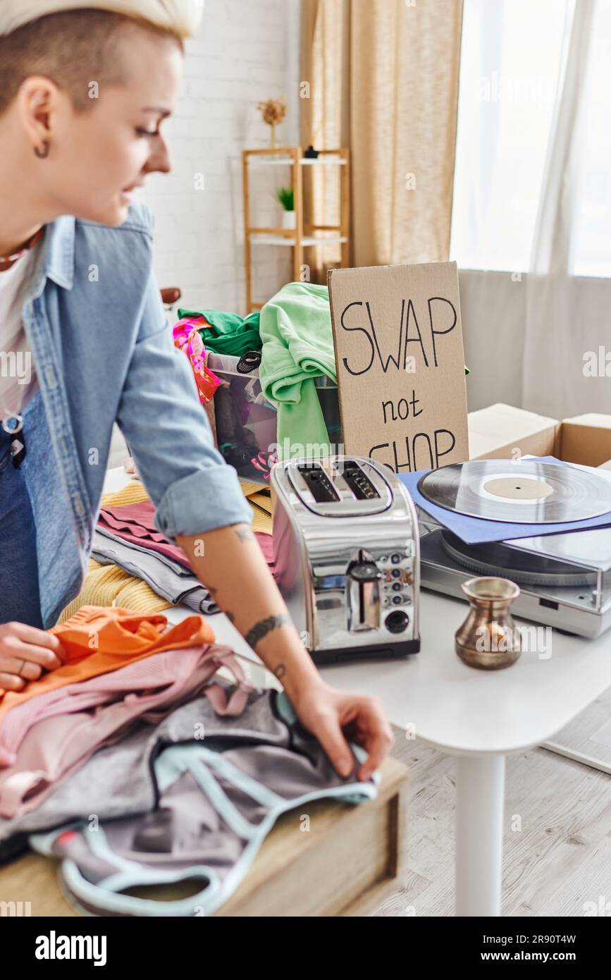 young woman sorting clothes near vinyl record player, electric toaster ...