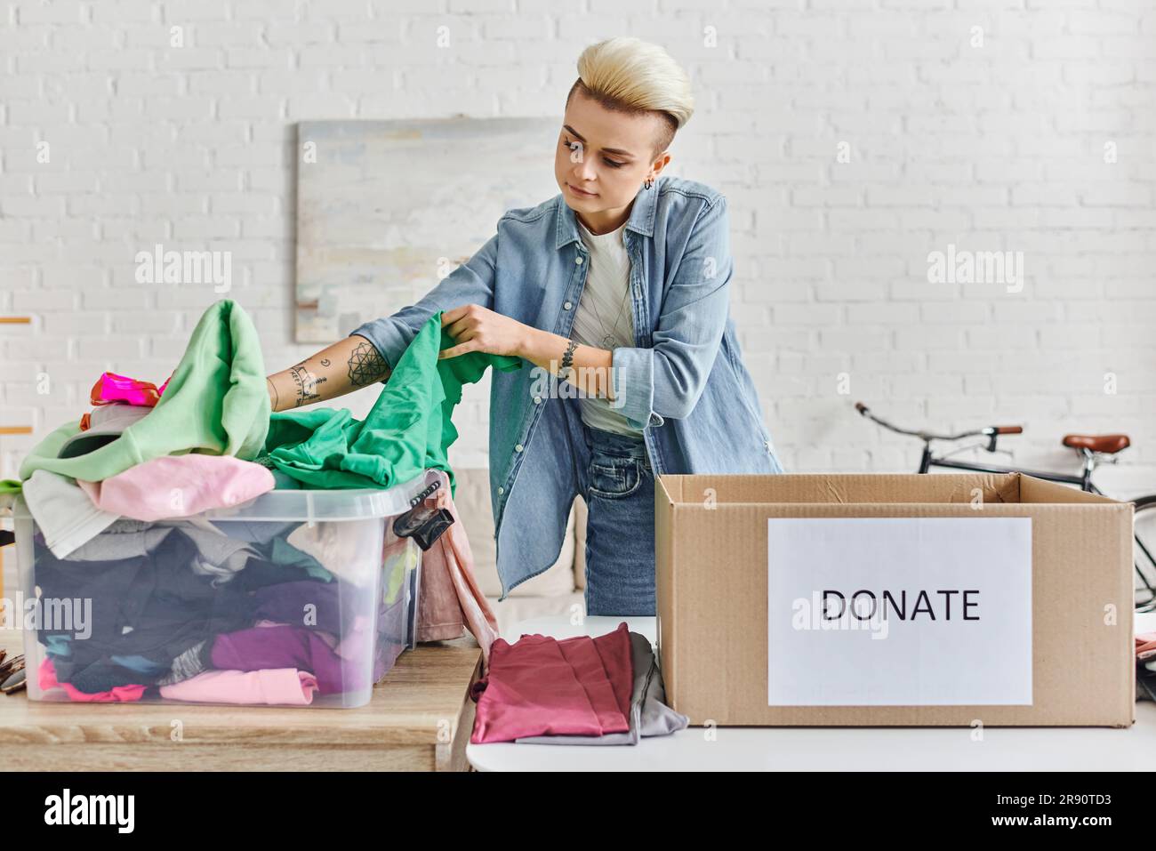 promoting social good, young tattooed woman sorting clothing in plastic ...