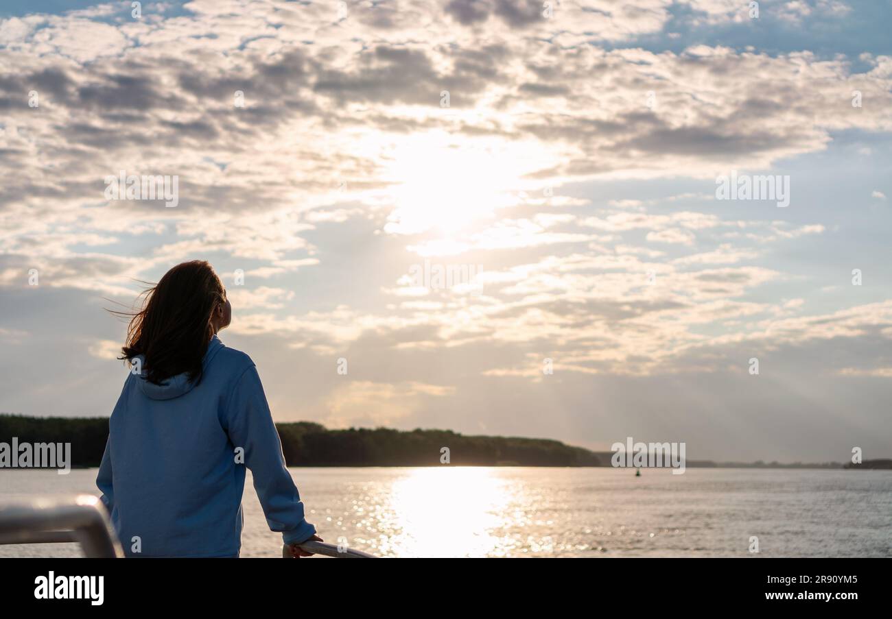 Woman standing on waterfront in front of river and enjoying sunset ...